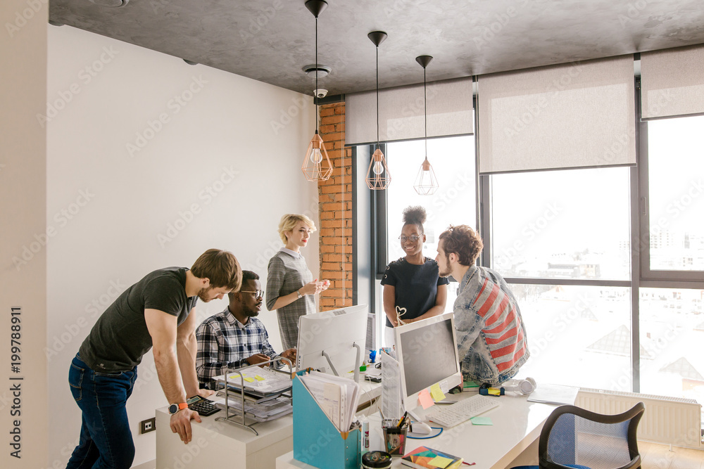 five young people are standing in the office and making plan of working ...