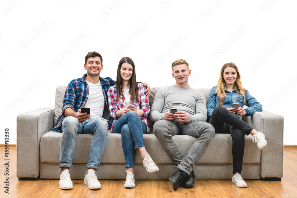 The four happy people with phones sit on the sofa on a white wall ...
