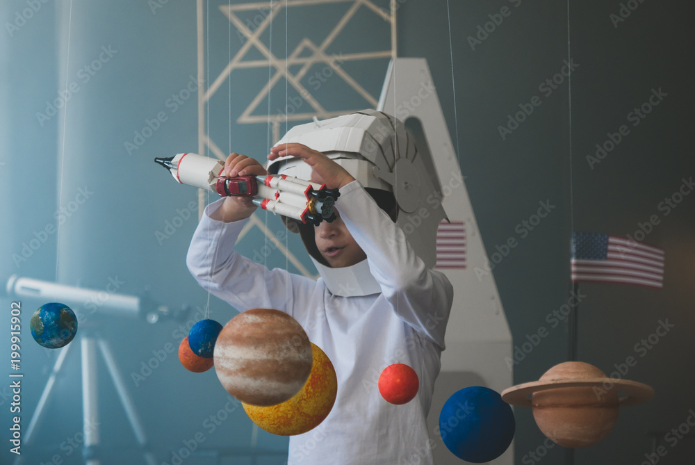 Cute little boy wearing cardboard astronaut helmet flying toy rocket ...
