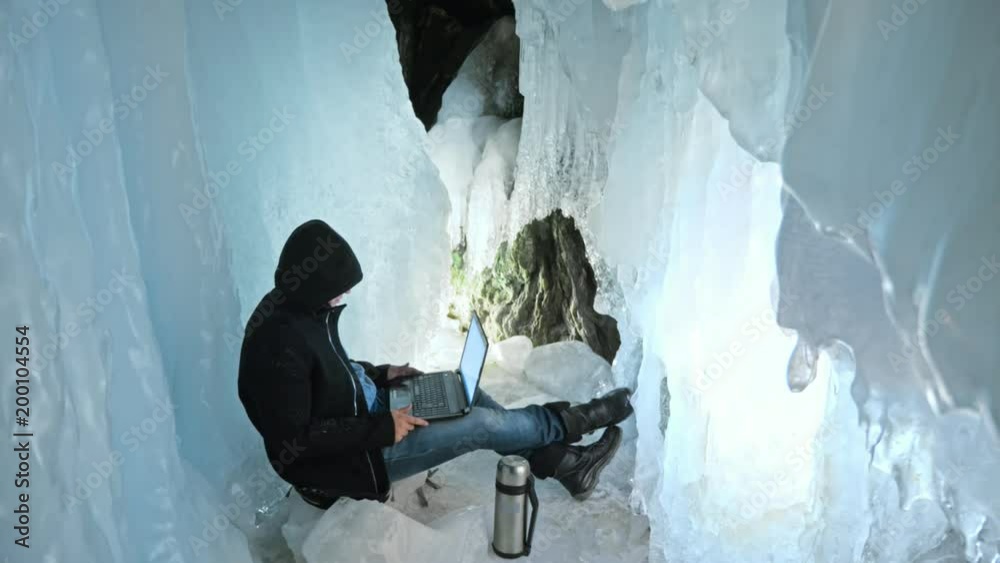 Hacker hacks the server. Man to program on laptop in ice cave. Around ...