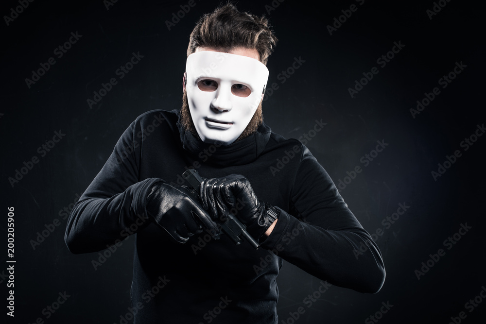 Robber in white mask and black clothes recharging his gun Stock 写真 ...