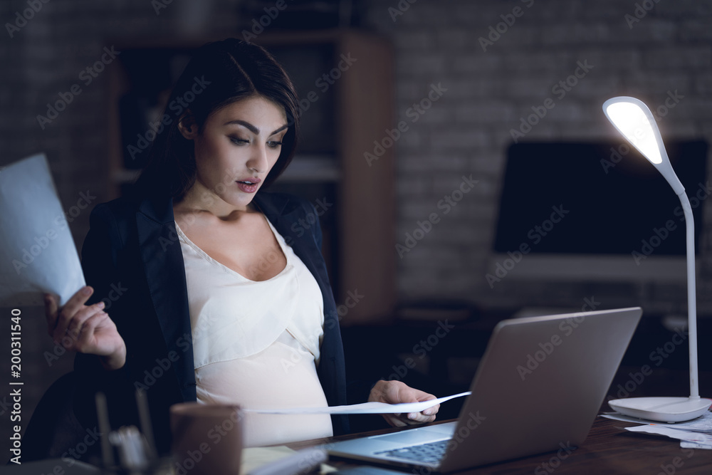 Surprised pregnant girl examines documents behind laptop. Pregnant in ...
