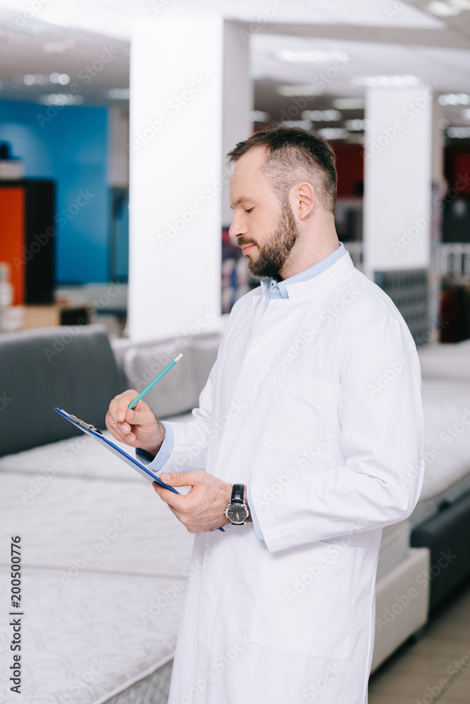 side view of shop assistant in white coat making notes in notepad in ...