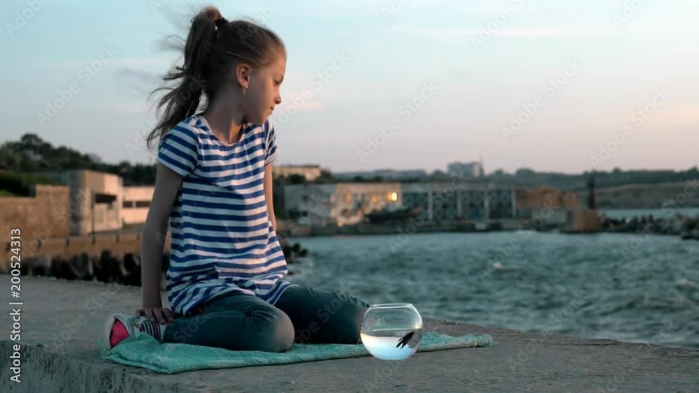 sad child girl seated on the coast with his fish a rounded aquarium ...