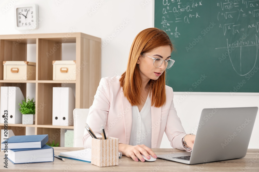 Beautiful young teacher with laptop sitting at table in classroom Stock ...