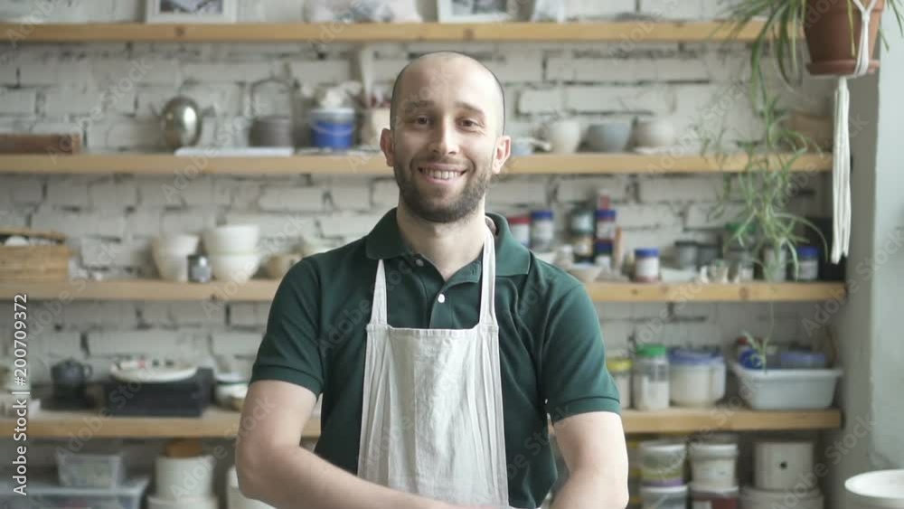 Portrait of male ceramist, who is standing in his studio and watching ...