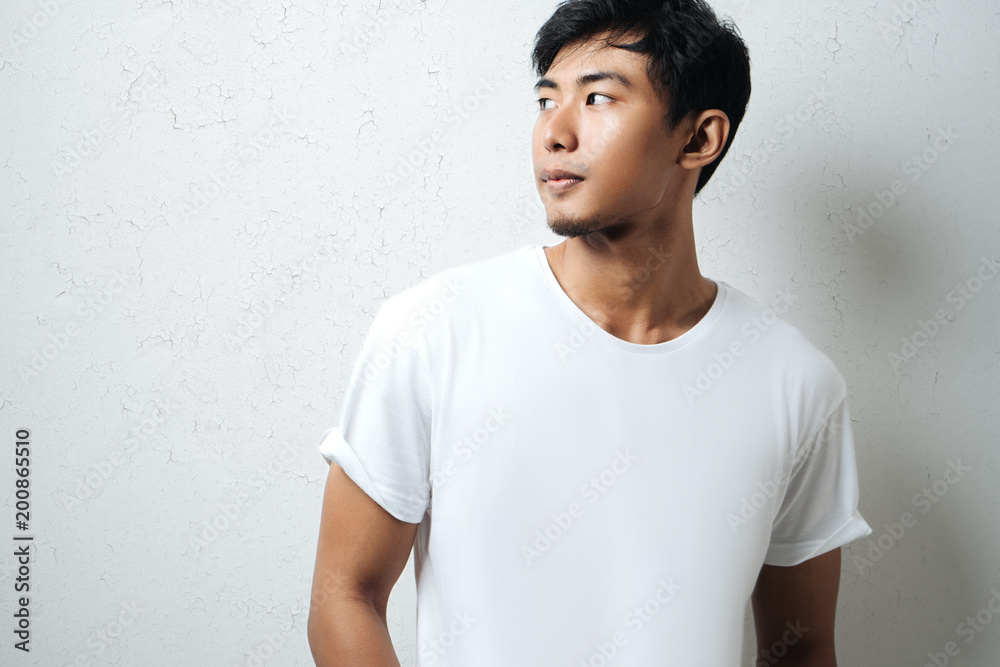 Handsome asian guy in white blank t-shirt, grunge wall, studio portrait ...