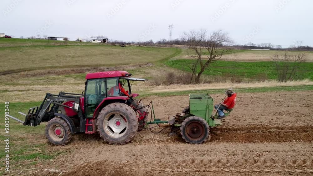 Aerial camera tracking a tractor with a potato planter moves through a ...
