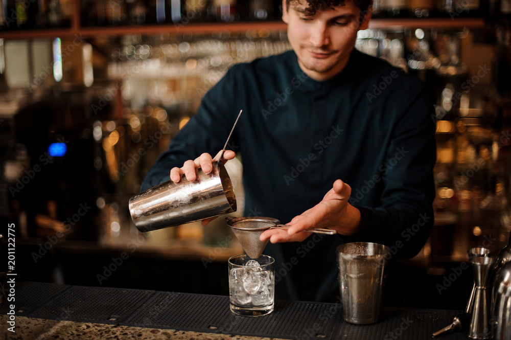 Bartender pouring an alcoholic cocktail into a glass from a steel ...