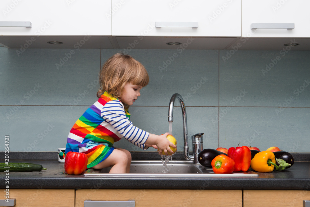Cute little child girl washing vegetables in a sink in a kitchen Stock ...