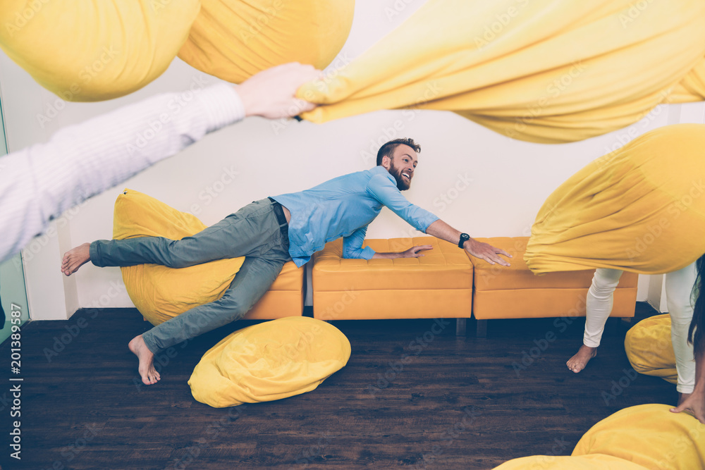 Cheerful Caucasian young man falling on couch to throw bean bag during ...
