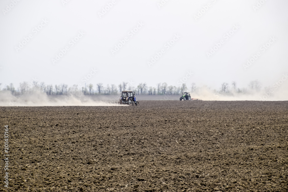 The tractor harrows the soil on the field and creates a cloud of dust ...