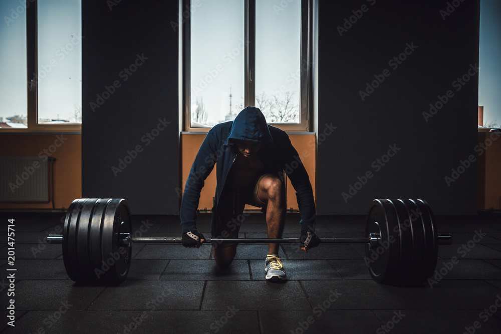 athletic man in jacket with a hood waiting and preparing before lifting ...