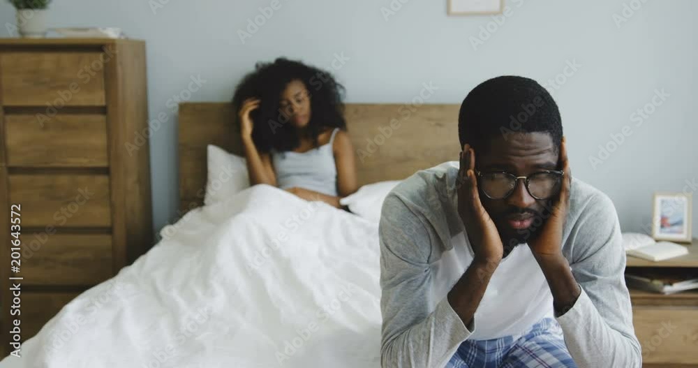 Sad young African American man in the pajama sitting on the corner of ...