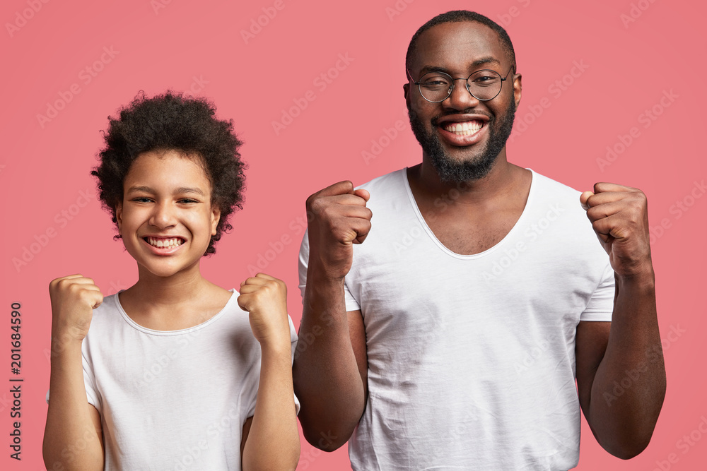 Happy dark skinned father and kid clench fists with great happiness and ...