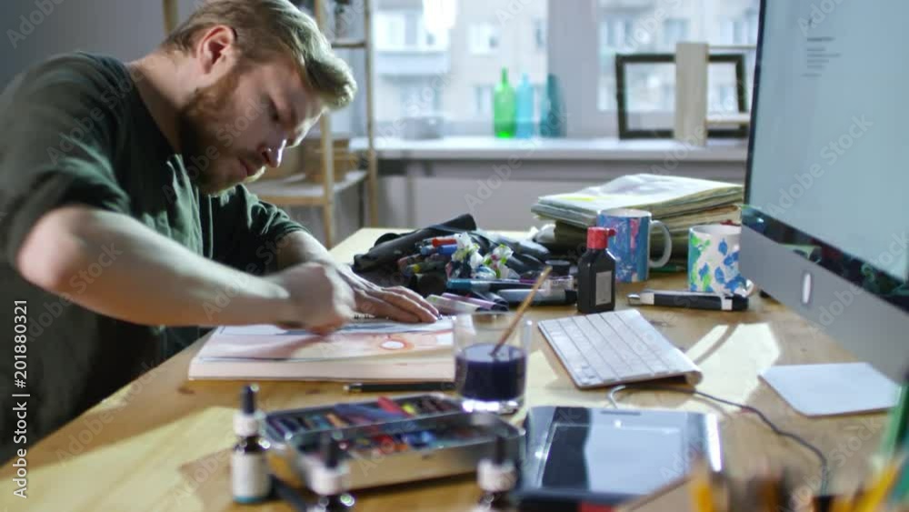 Tilt up shot of young bearded man drawing picture in sketchbook and ...
