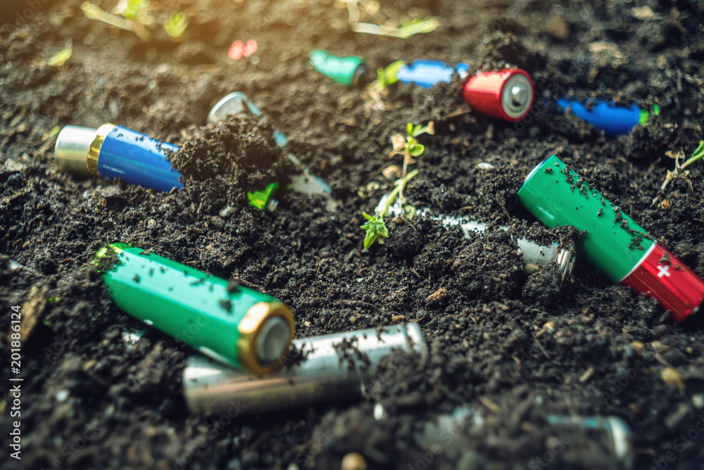 Used alkaline batteries lie in the soil where plants grow. Concept of ...