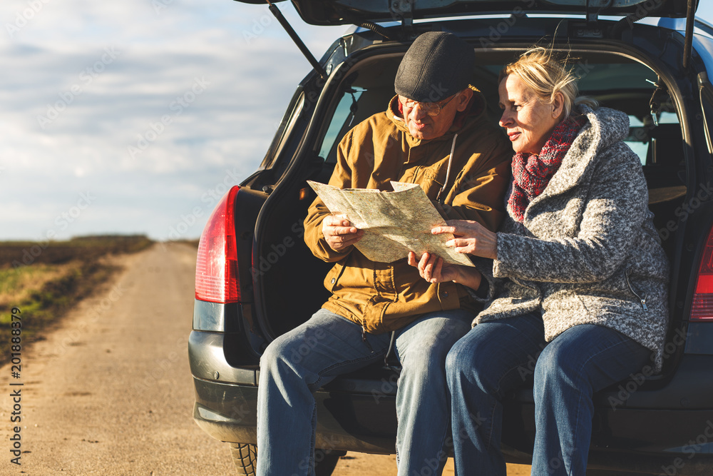Happy senior couple on a road trip, they are using map for direction ...