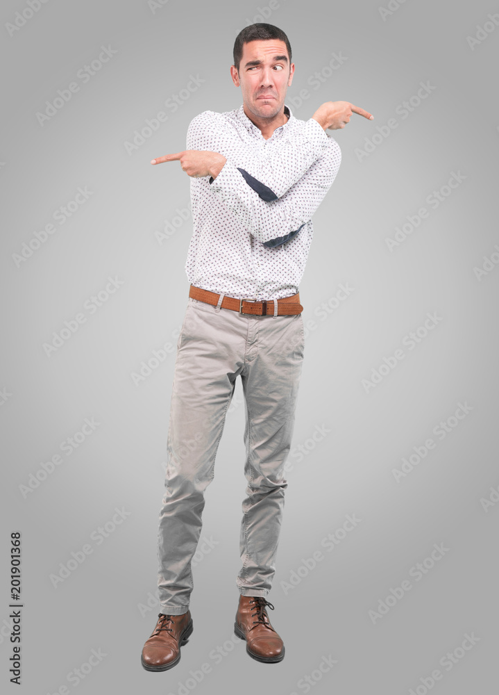 Puzzled young man pointing in one direction and the opposite - Full ...