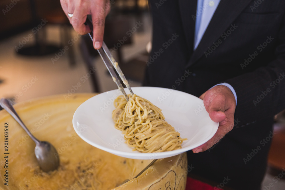 Chef neatly plating spaghetti carbonara in cheese wheel on white plate ...