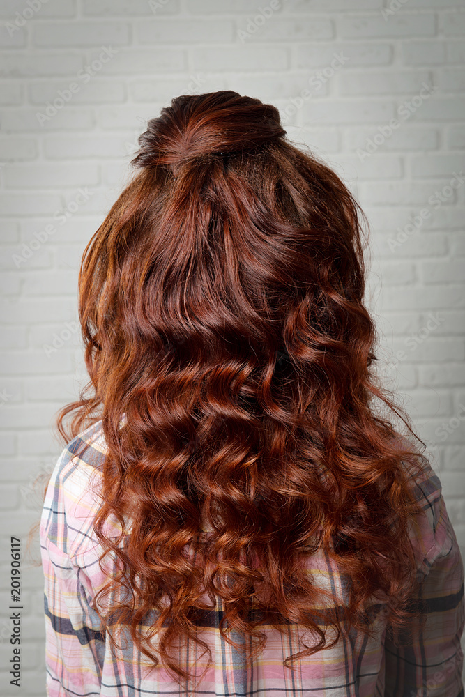 Hairstyle long curls on a red-haired girl back view on a light ...