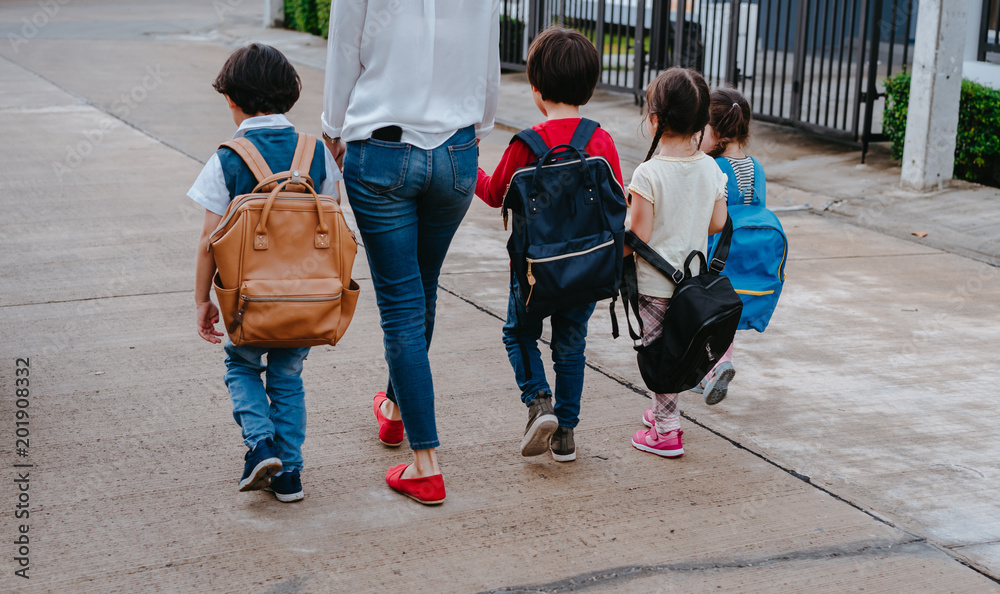 Mother and pupil and kids holding hands going to school in first class ...