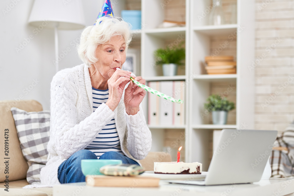 Ecstatic senior woman in party hat blowing horn while celebrating ...