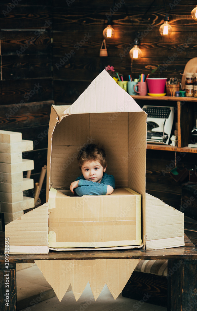 Kid sit in cardboard hand made rocket. Boy play at home with rocket ...