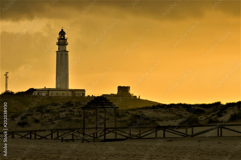 dorado atardecer con el faro de trafalgar de fondo en la playa de caños ...
