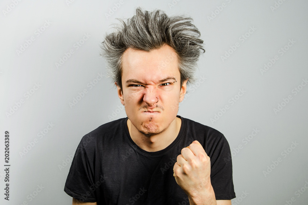 Unshorn and unshaven young guy with piercings on his face in rage shows ...
