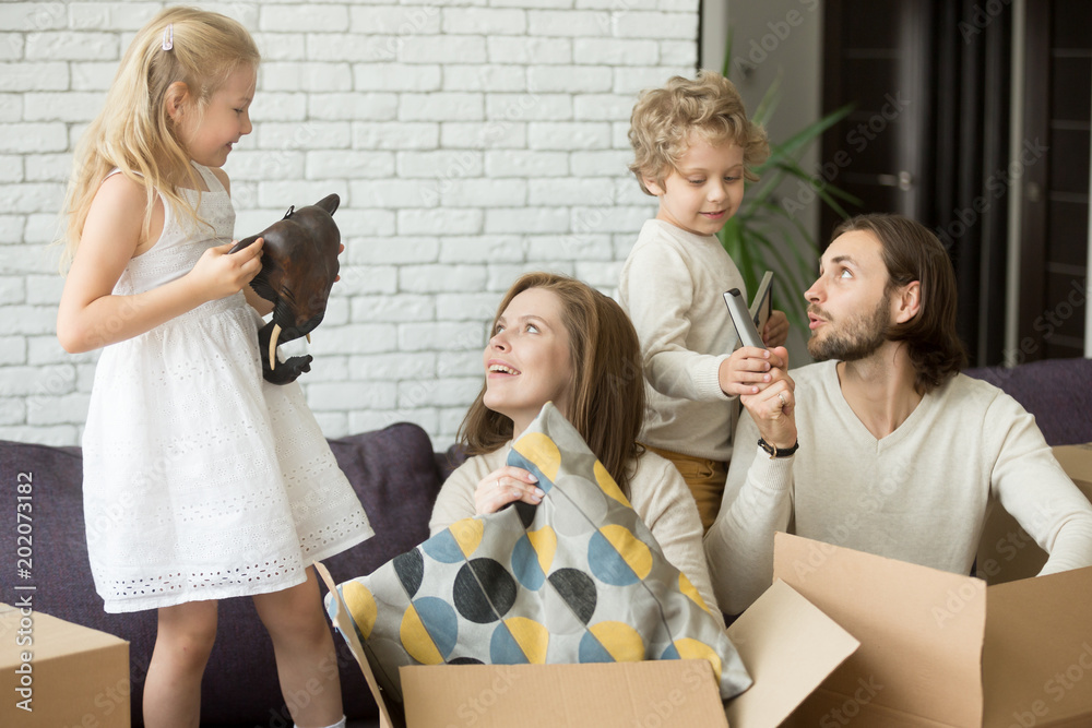 Happy children helping parents to unpack boxes in new home on moving ...