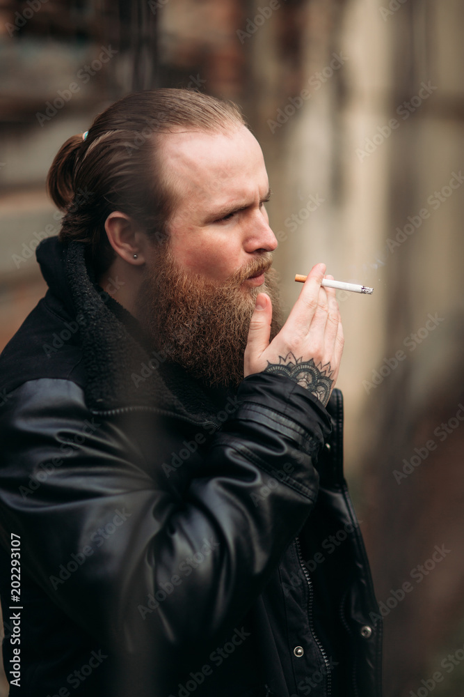 A bearded man in a black leather jacket stands outside and poses for a ...