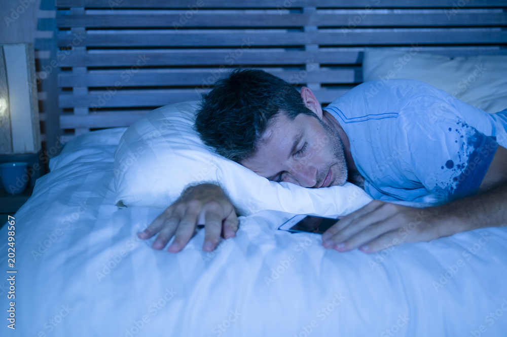 attractive tired man in bed falling asleep while using mobile phone ...