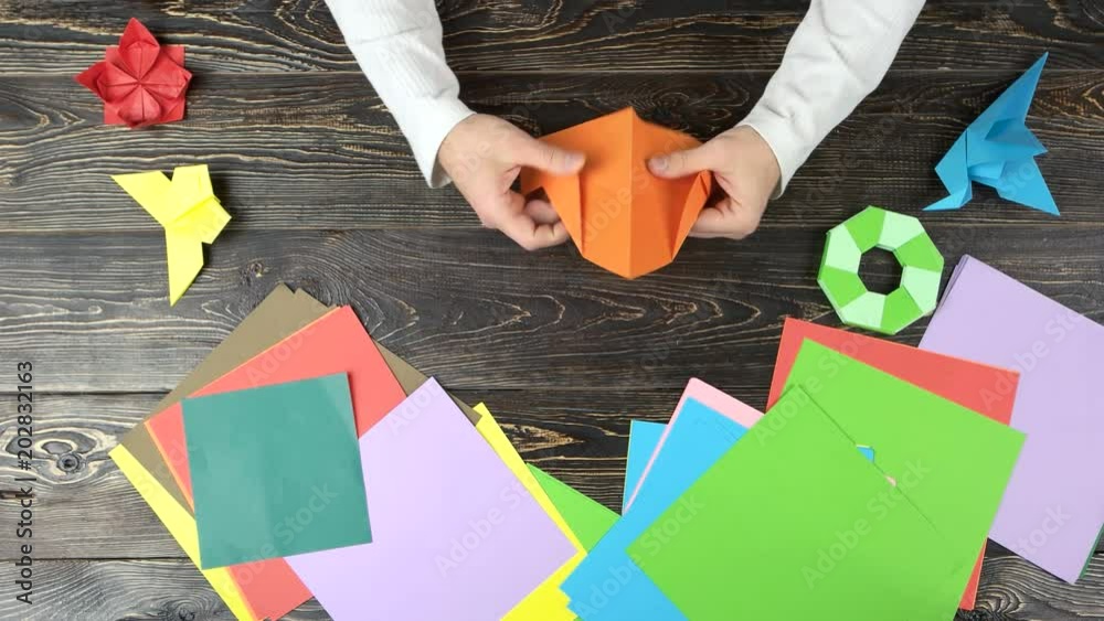 Man folds paper sheets while doing origami. Different origami objects ...