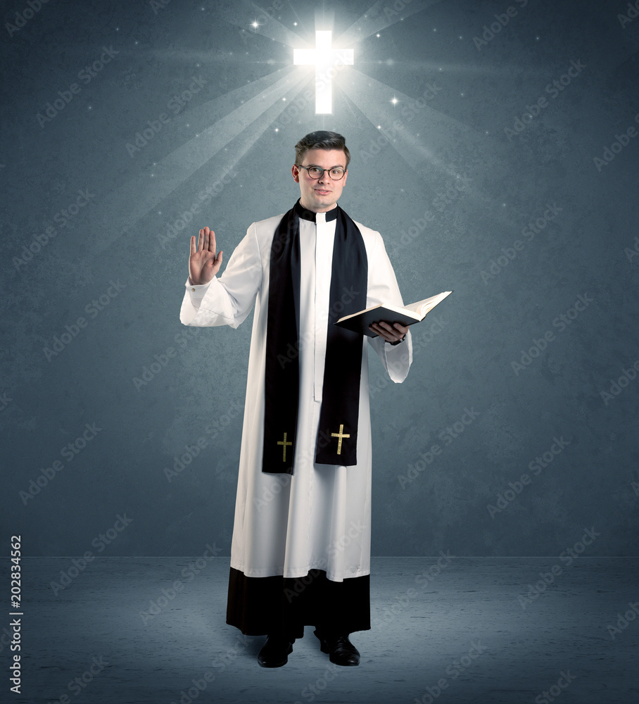 A young caucasian priest with deep faith blessing with the holy bible ...