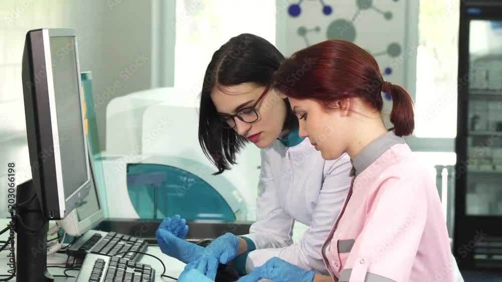 Young female laboratory workers using computer together conducting ...