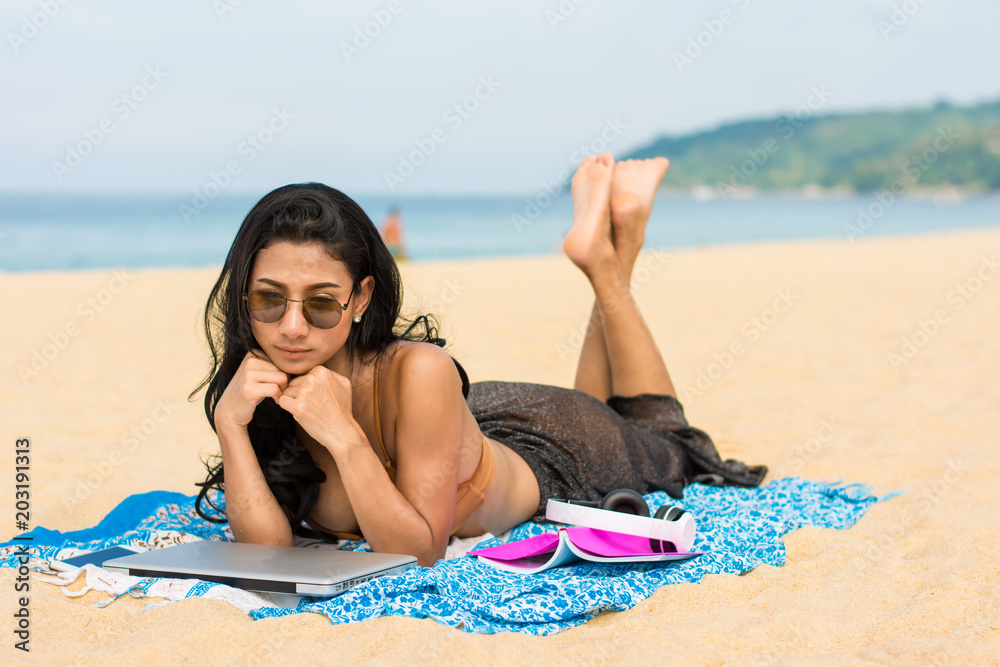 Sexy asian woman sunbathing on the beach with laptop , mobile phone While relaxing on weekends ...