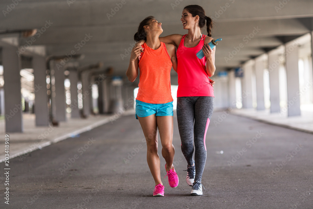 Couple of female friends jogging on the city street under the city road ...
