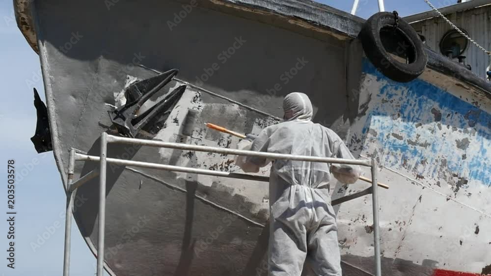 Worker paints with brush metal front of ship at shipyard in port of ...