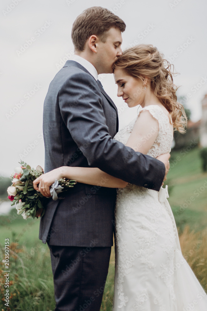 Handsome groom embracing beautiful bride and kissing her on the ...