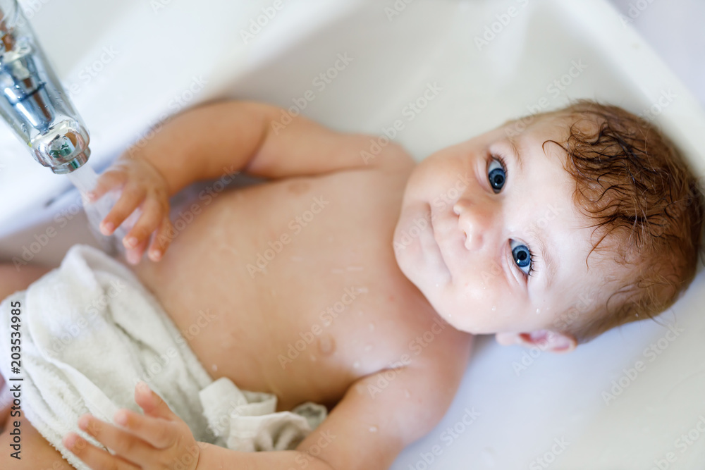 Cute adorable baby taking bath in washing sink and grab water tap ...