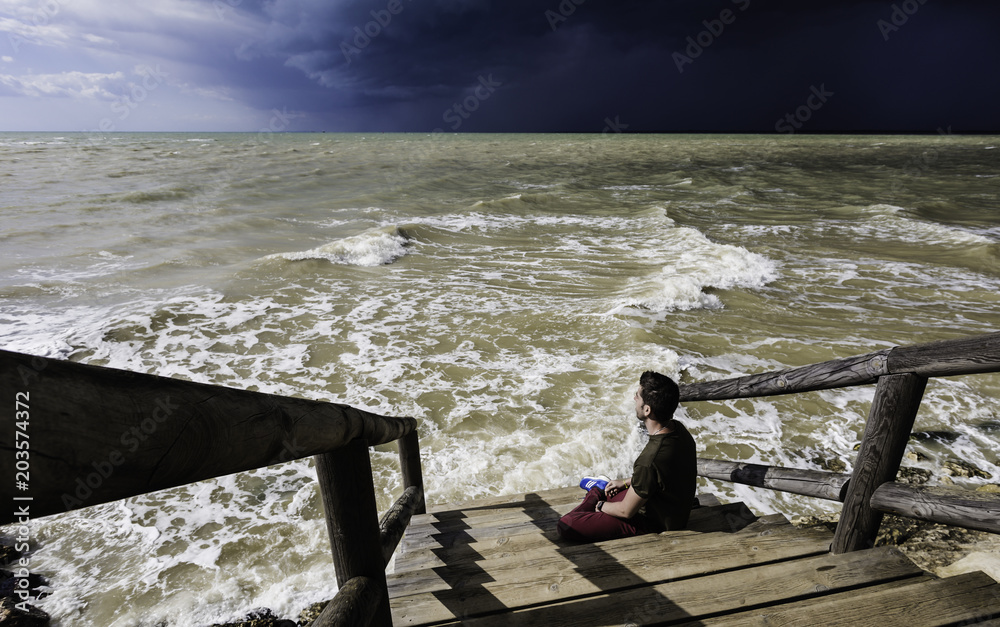 Hombre joven sentado en el muelle de madera frente al mar en Stock ...