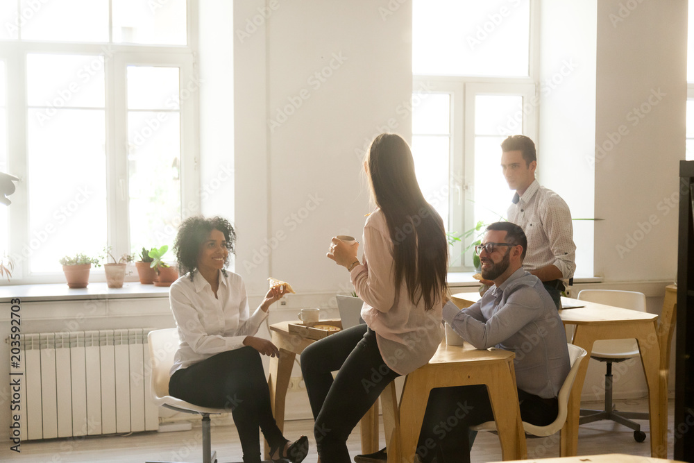 Smiling multiracial colleagues talking eating pizza at lunch in office ...