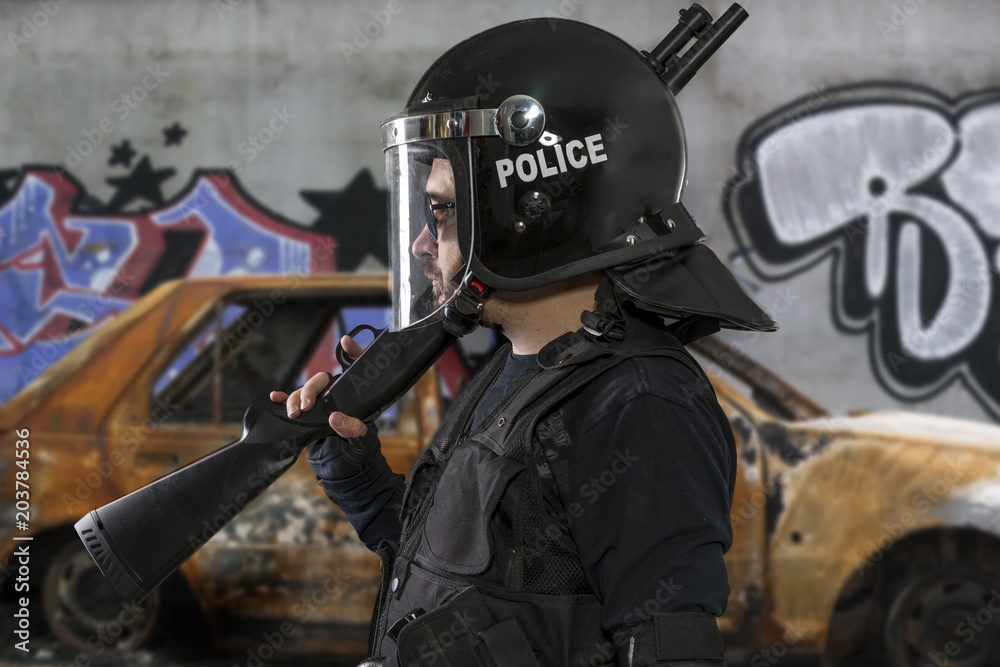 armed police with riot helmet and vest in a scene with a burnt car and ...
