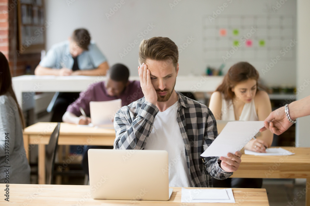 Upset male student looking sadly at given paper, unsatisfied with exam ...