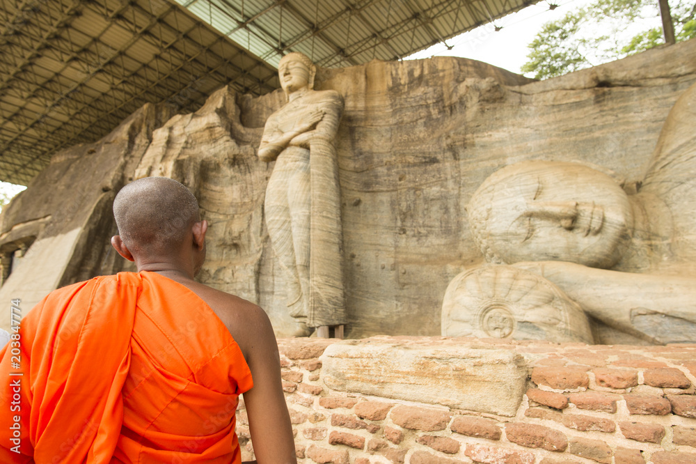 A monk is walking in front of the statue of Reclining Buddha and Monk ...