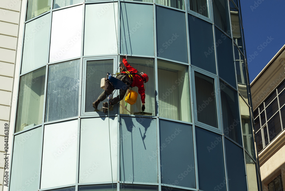 rope access technician in a helmet washes the window of a high-rise ...