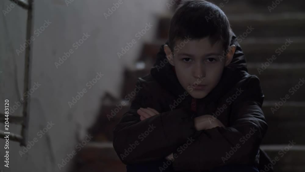 boy sits alone in an old ramshackle building and looking to the camera ...