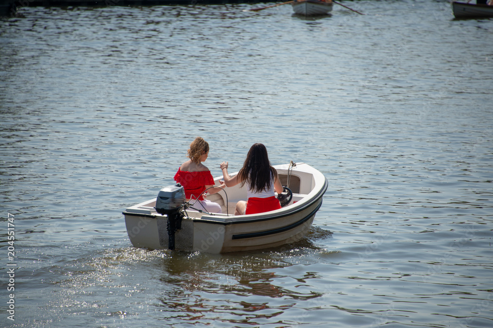 two girls in red and white outfits driving motor boat on river in in ...