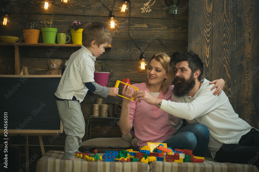 Parents hug each other while playing with kid. Side view standing blond boy taking plastic ...